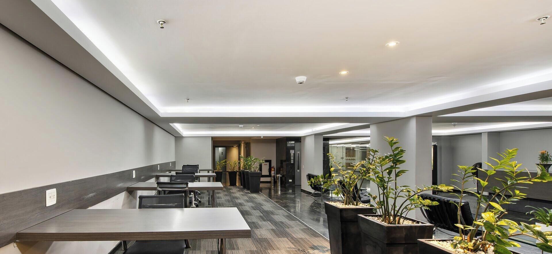 Um saguão de hotel moderno com um balcão de recepção extenso, área de estar e plantas em vasos.