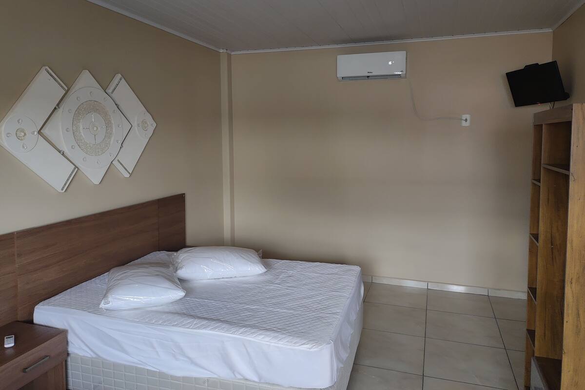 Quarto com cama, mesa de cabeceira, ar condicionado fixado na parede e televisão na parede.
