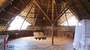 Um quarto espaçoso com teto alto de madeira, uma cama, uma cadeira e uma mesa.