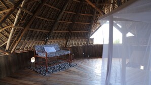 Um quarto com telhado de palha, cama com roupa de cama estampada e tapete de palha no chão.