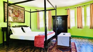 Uma cama com dossel com um cobertor vermelho, uma mesa pequena com abajur e uma pintura grande na parede.
