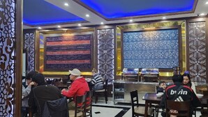 Interior de restaurante com design moderno, apresentando paredes estampadas e uma área de estar com mesas e cadeiras.