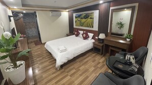Quarto de hotel com cama, escrivaninha com cadeira, mesinha de cabeceira com abajur, espelho e planta em vaso.