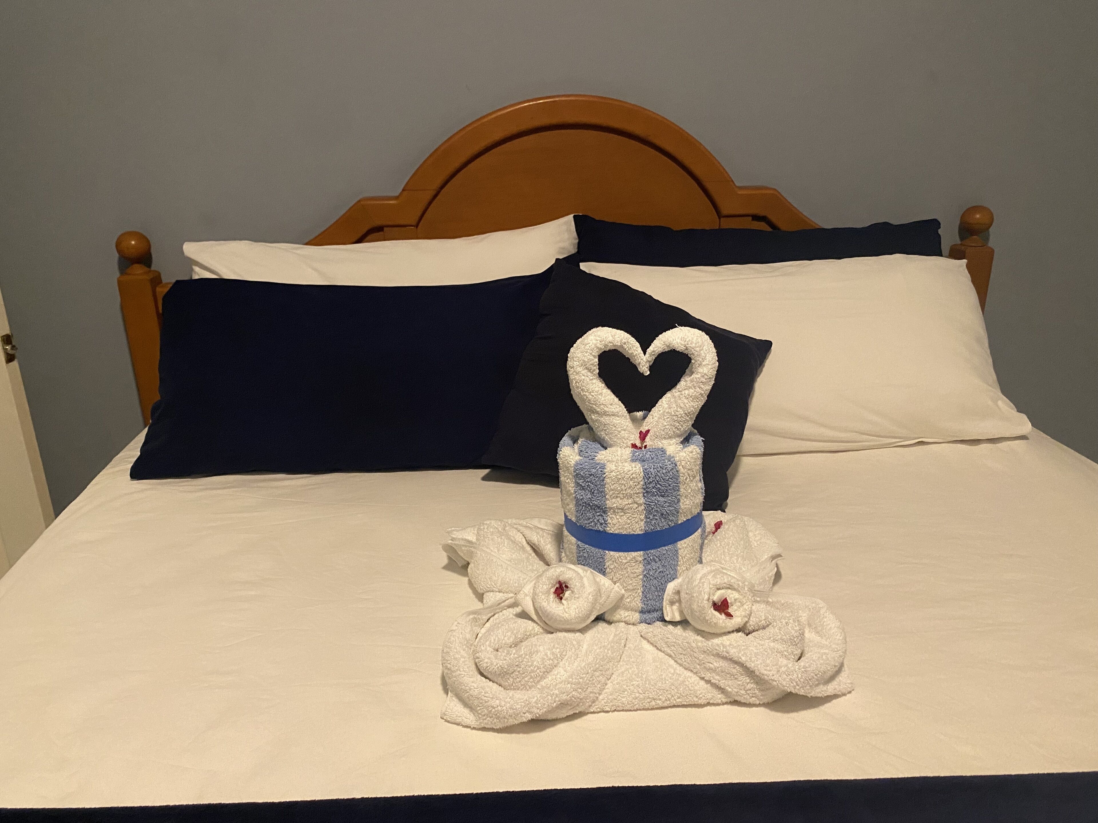Uma cama bem arrumada com arranjo de toalhas em formato de coração, uma toalha listrada e dois toalhas em formato de coração.