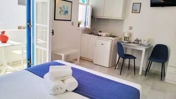 Quarto de hotel com cama, pequeno espaço de cozinha, escrivaninha e uma cadeira.