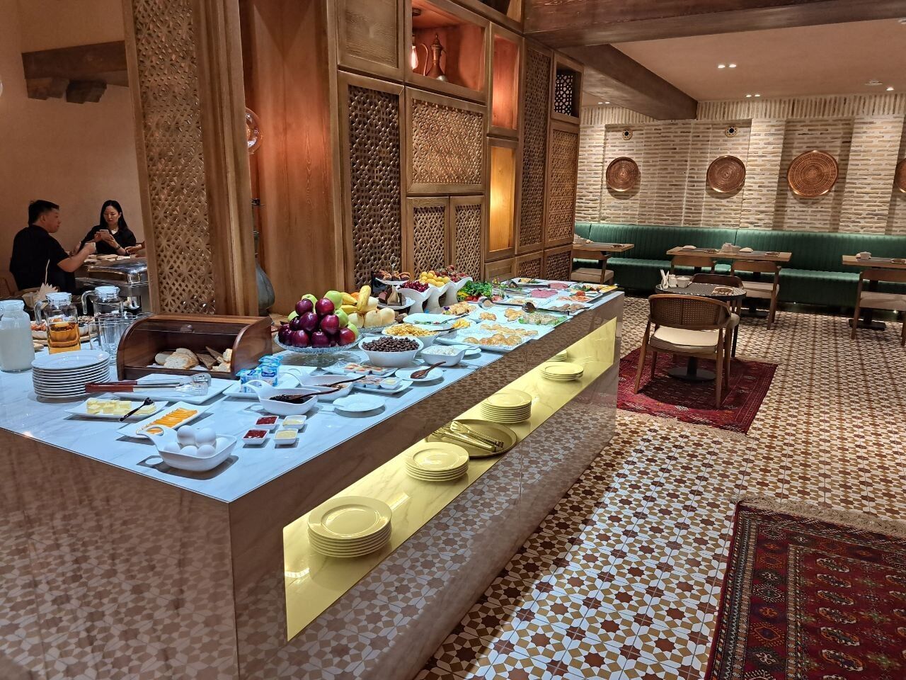 Disposição de buffet com diversos alimentos e área de estar com cadeiras estofadas em verde.