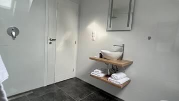 Uma casa de banho moderna com uma porta branca, um espelho grande, uma prateleira de madeira com toalhas e uma sanita branca.