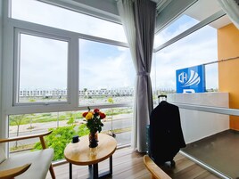 Varanda com vista para edifícios e vegetação, uma mesa com um vaso de flores e uma mala.