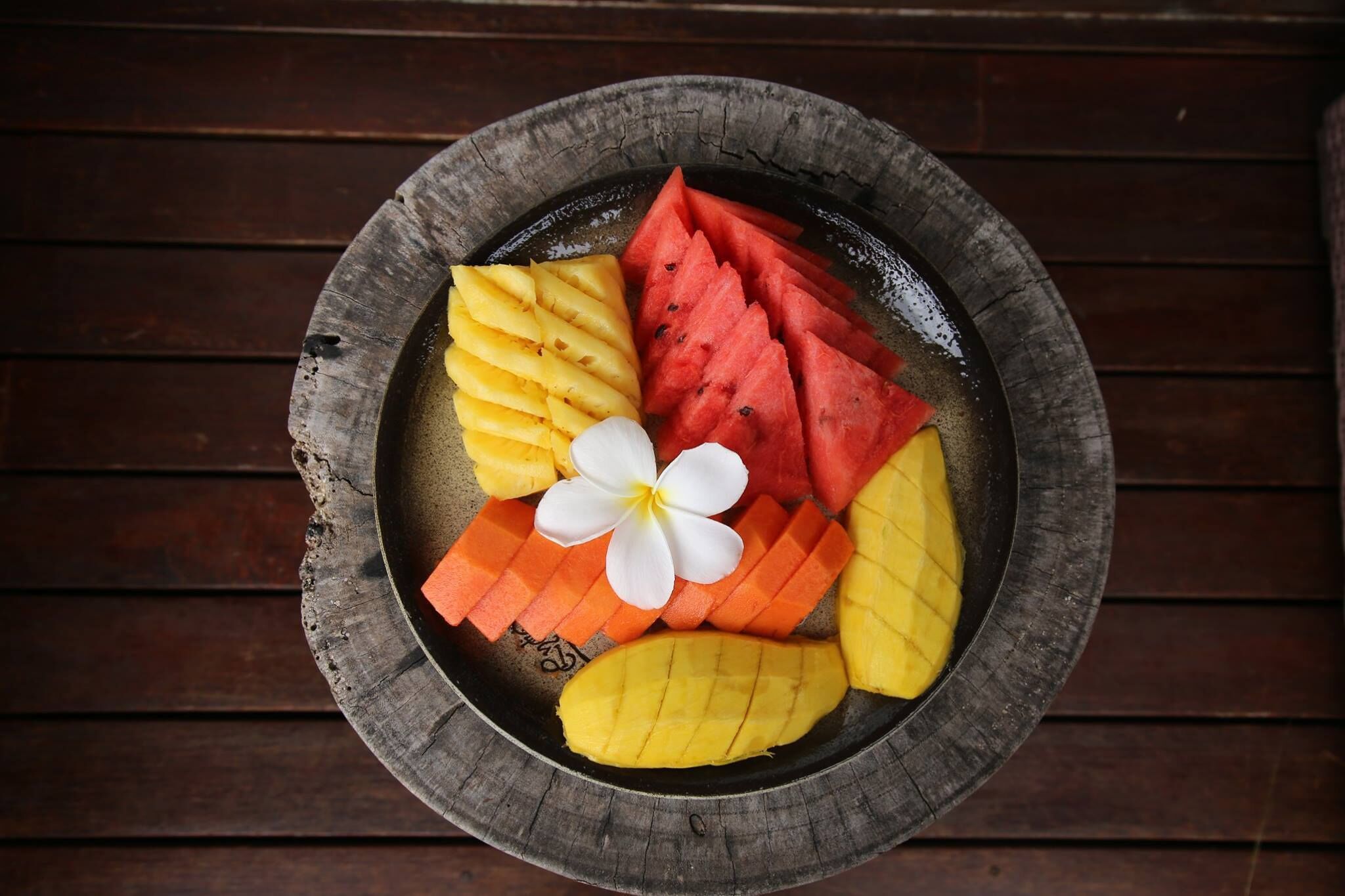Uma tigela de madeira com frutas fatiadas e uma flor.