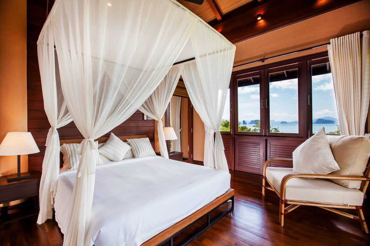 Quarto com cama de dossel, chaise longue e vista para o mar.