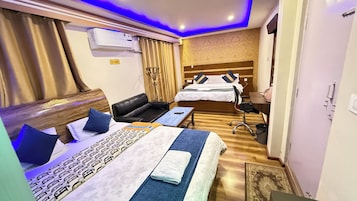 Quarto de hotel com duas camas, uma escrivaninha, uma cadeira, um sofá e um ar condicionado.