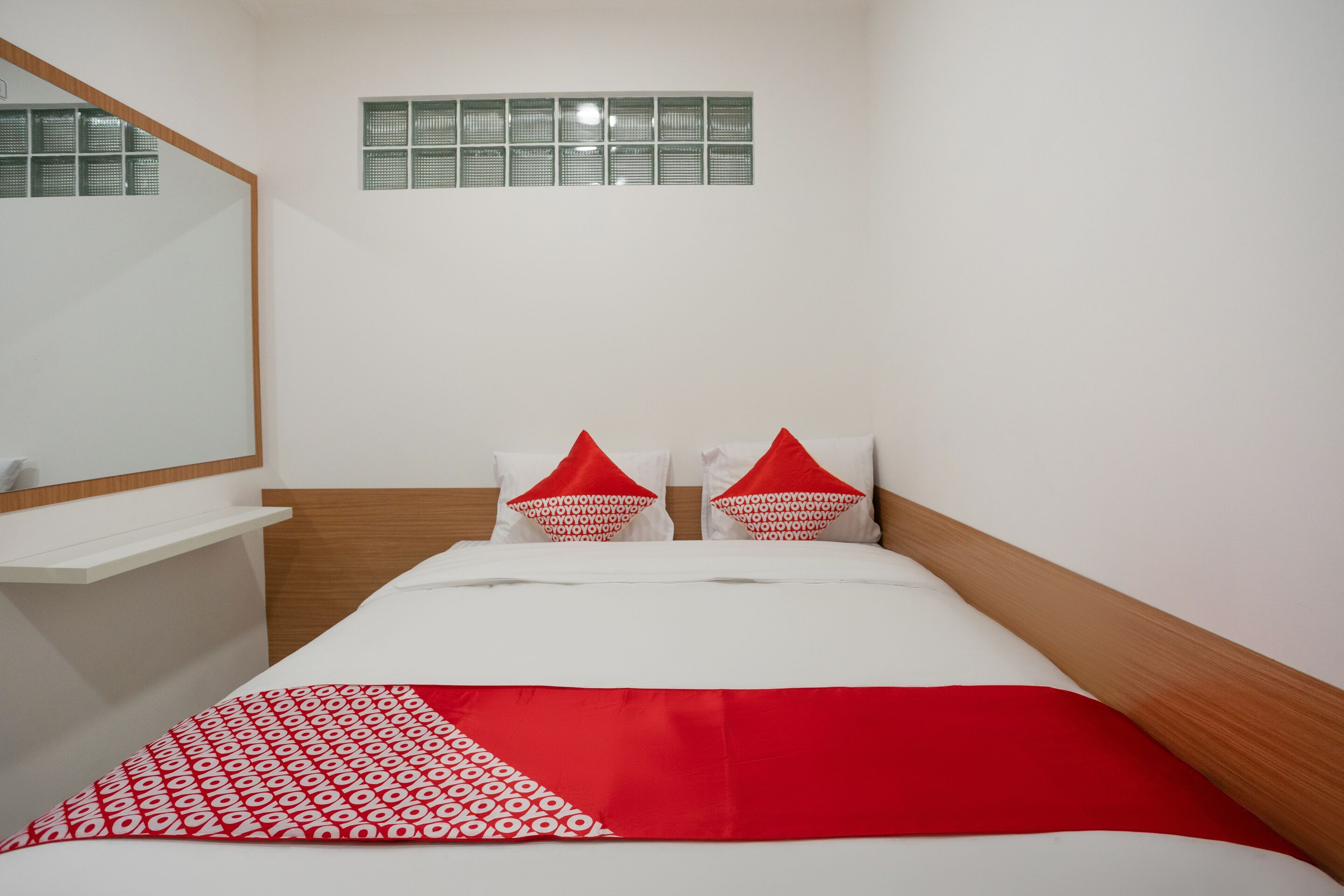 Quarto de hotel com cama, cabeceira de madeira, parede branca, janela com persianas e espelho.