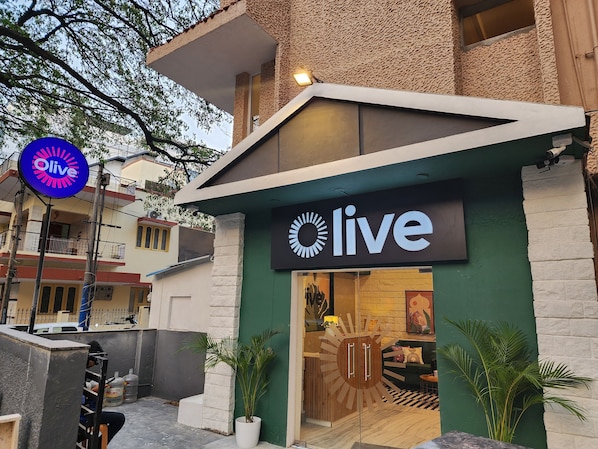 Um edifício com placa indicando 'live', entrada moderna e plantas em vasos.