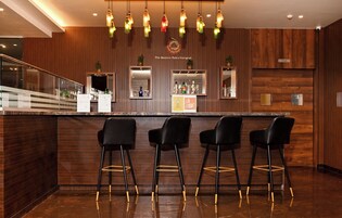 Uma área de bar moderna com estilo retrô, painéis de madeira, um balcão e três banquetas pretas.