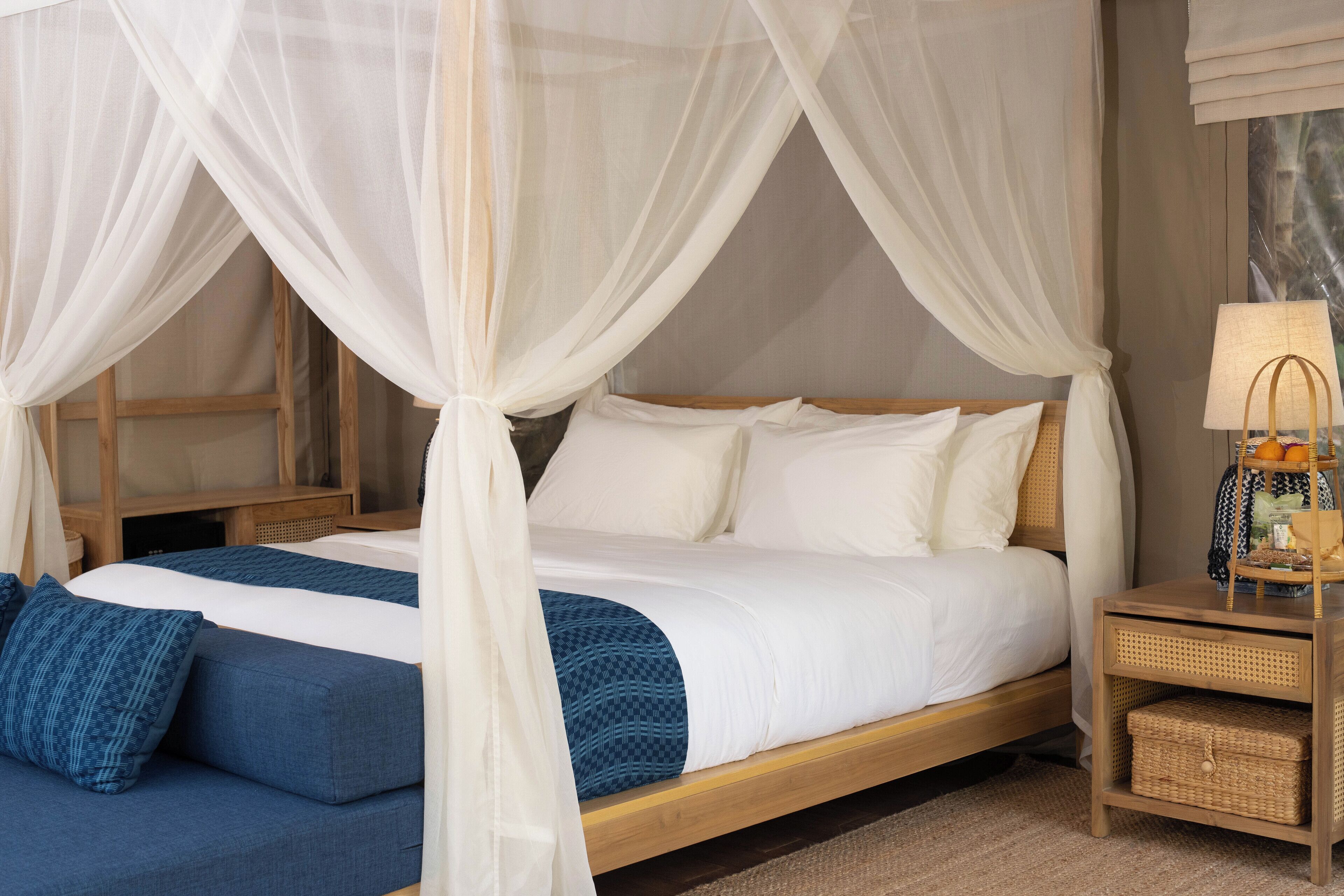 Quarto com cama de dossel, mesa de cabeceira com abajur e um sofá azul.