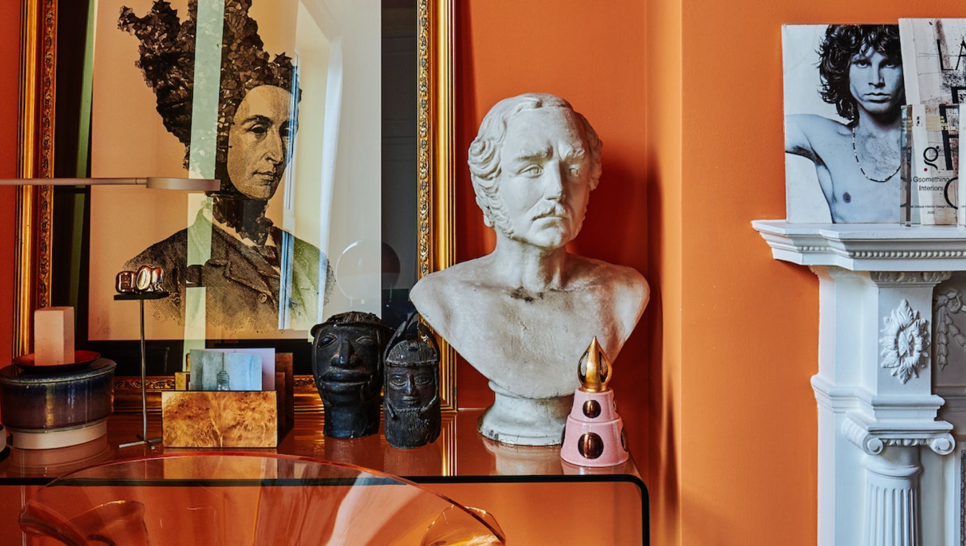 Um quarto com um busto de mármore, um retrato emoldurado e uma lareira com parapeito.