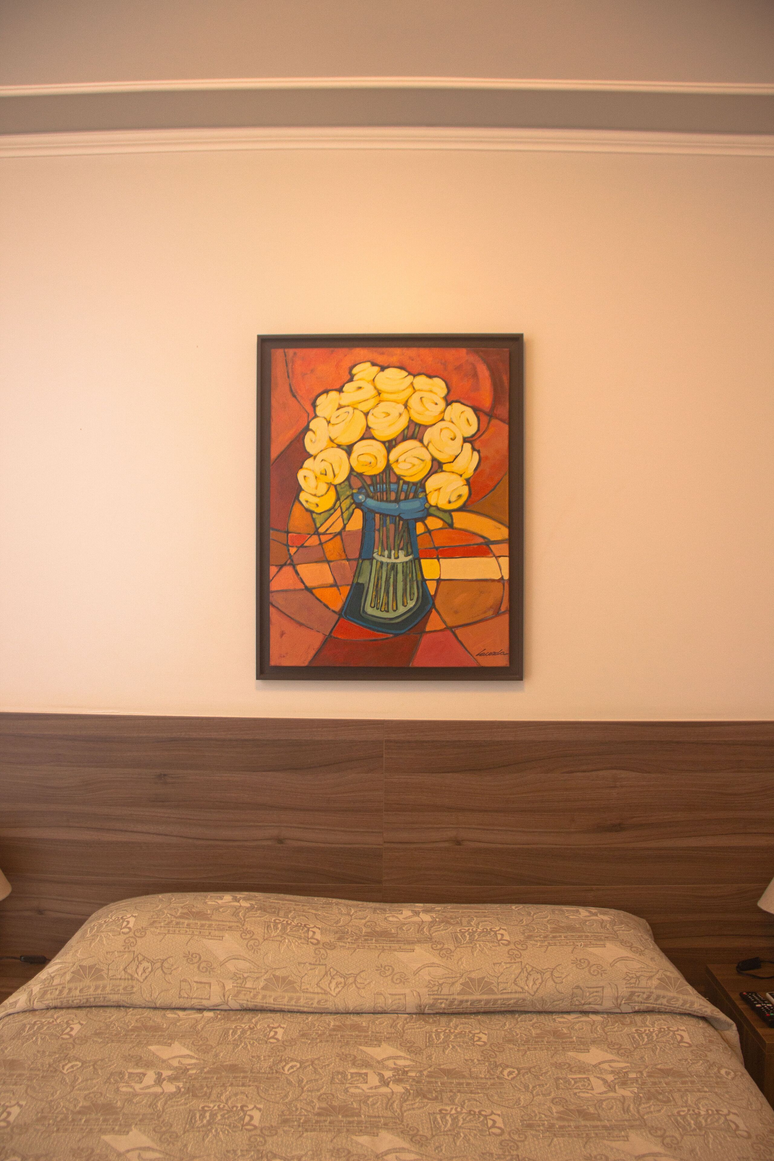 Um quarto com uma cama, um quadro na parede com flores amarelas e uma cabeceira de madeira.