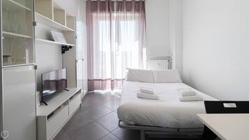 Quarto de hotel moderno com uma cama, uma televisão em um suporte, uma estante com uma moldura e uma janela com cortinas.