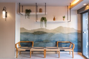 Quarto com duas cadeiras de madeira, prateleira com plantas na parede e uma grande pintura abstrata.