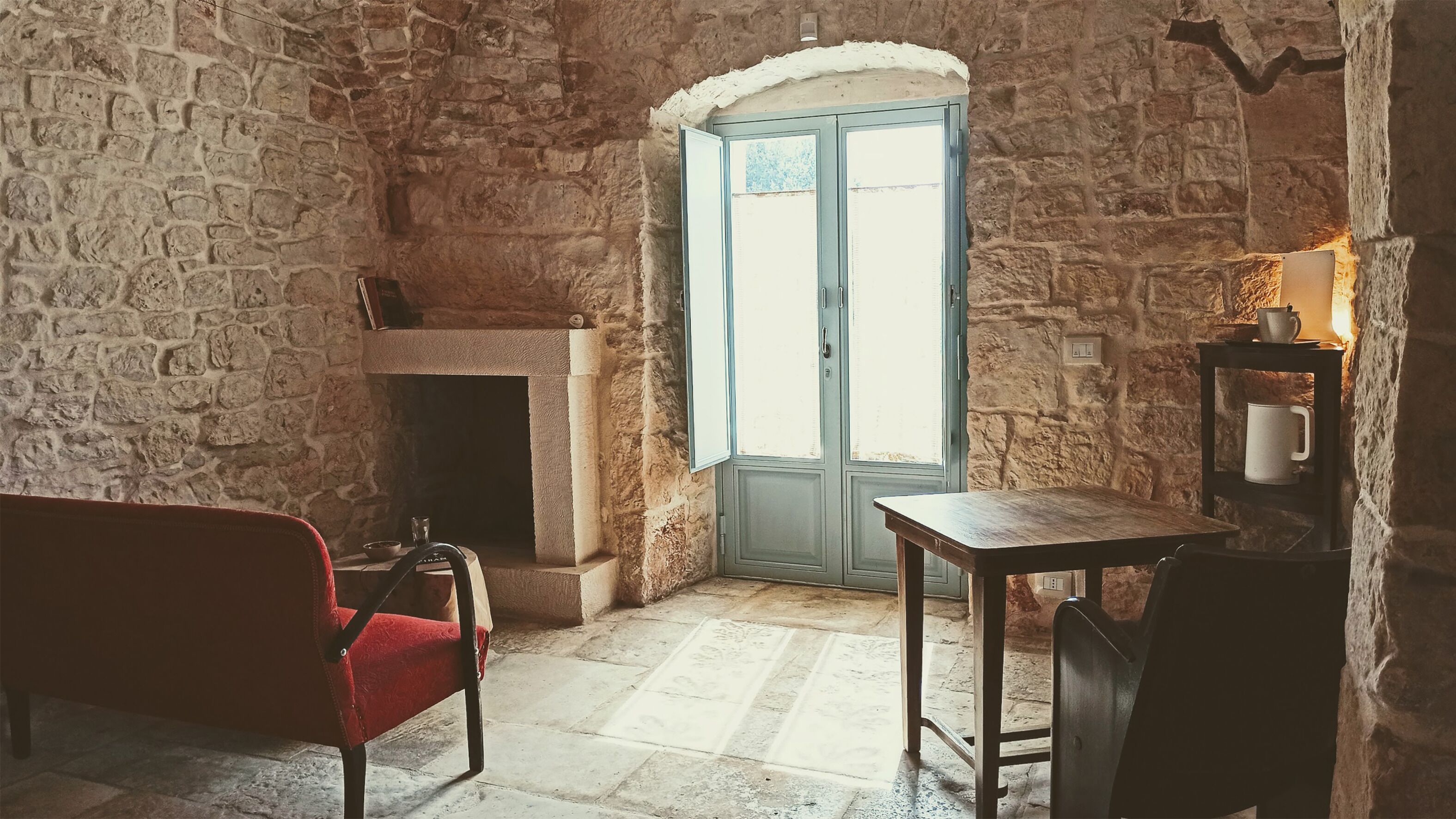 Um quarto rústico com paredes de pedra, lareira, uma porta azul e uma mesa com cadeiras.