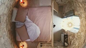 Quarto com uma cama, uma mesinha, prateleira na parede e janela com vista.