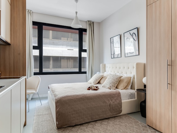 Quarto moderno com cama, mesa de cabeceira e janela com cortinas.