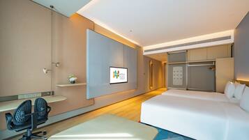 Quarto de hotel com cama, escrivaninha, cadeira, guarda-roupa e um pequeno prateleira com uma flor.