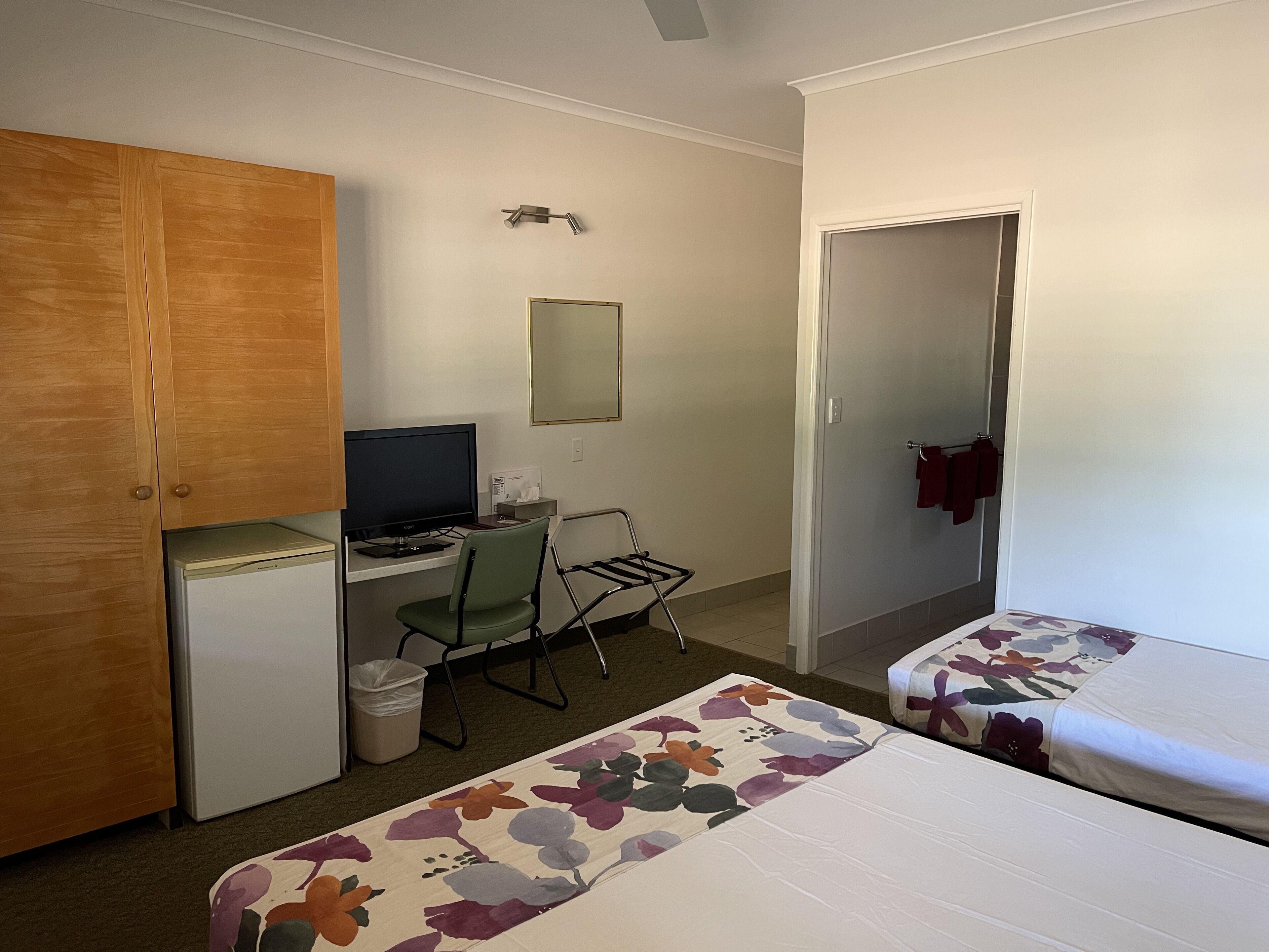 Quarto de hotel com escrivaninha, computador, cadeira e duas camas.
