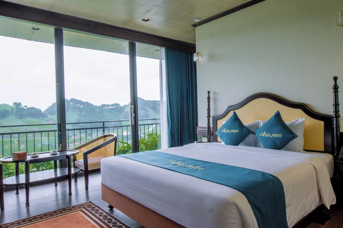 Quarto de hotel com uma cama grande, vista para o exterior, uma pequena mesa com cadeira e varanda.