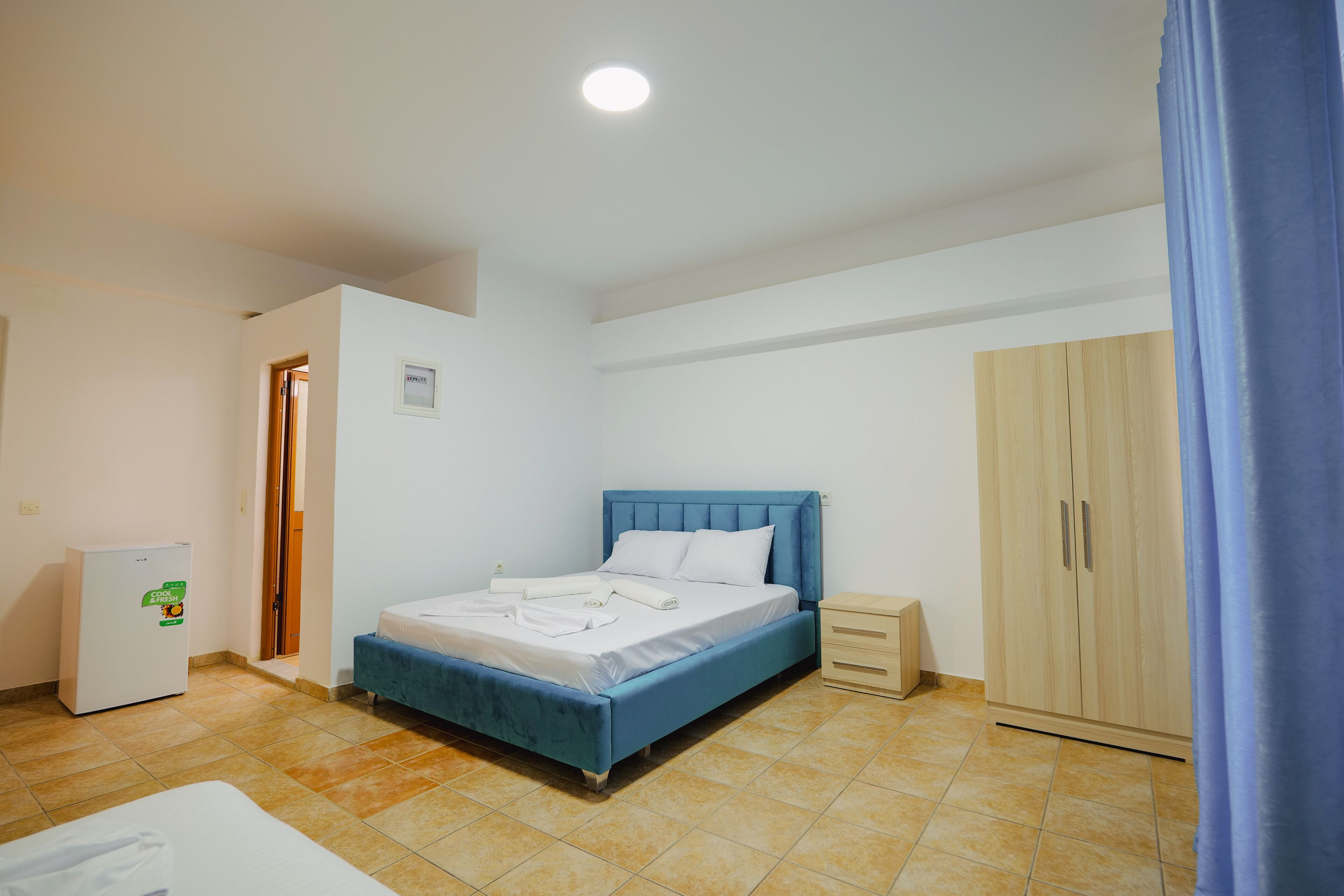 Um quarto com cama, guarda-roupa, mesa de cabeceira e frigorífico.
