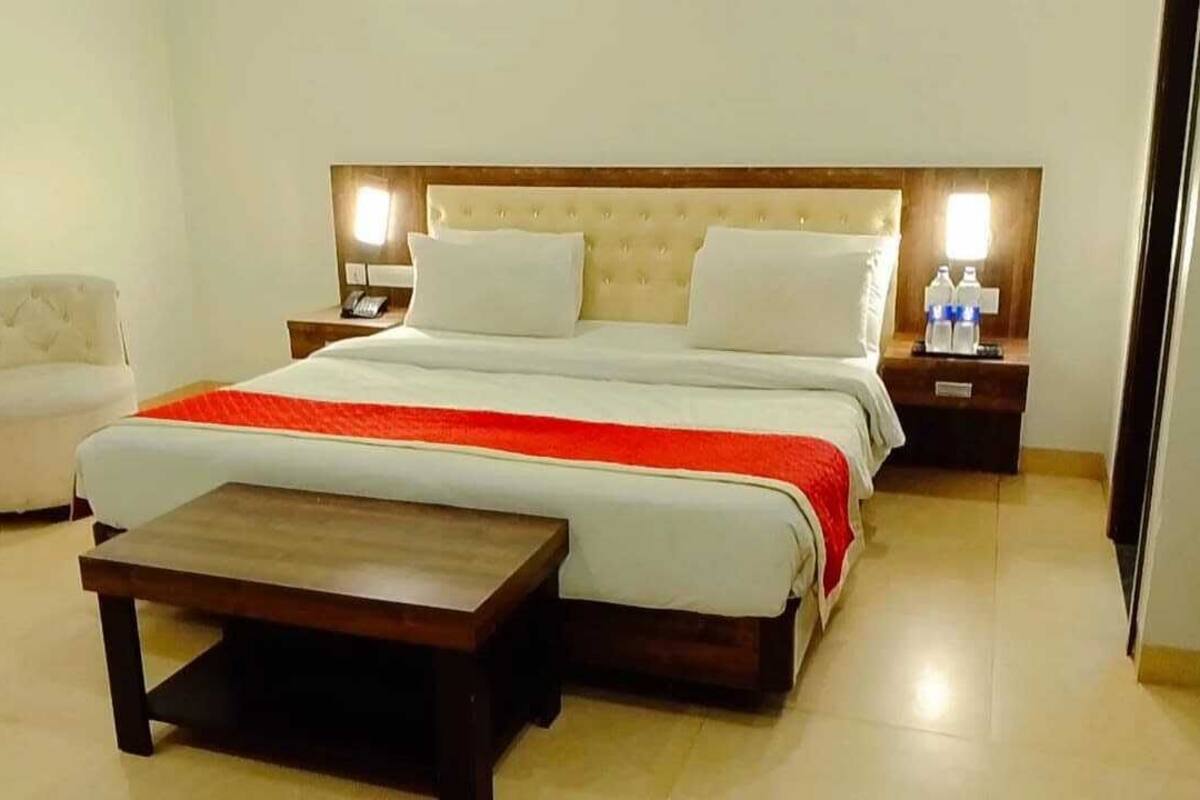 Quarto de hotel com uma cama grande, uma mesa de cabeceira, uma cadeira e uma mesinha.