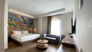 Quarto de hotel com cama, sofá, mesa de centro redonda e televisão.