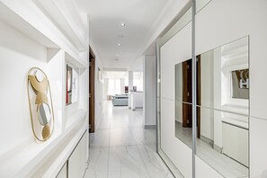 Um corredor de hotel moderno com paredes brancas, piso de mármore e um espelho grande.