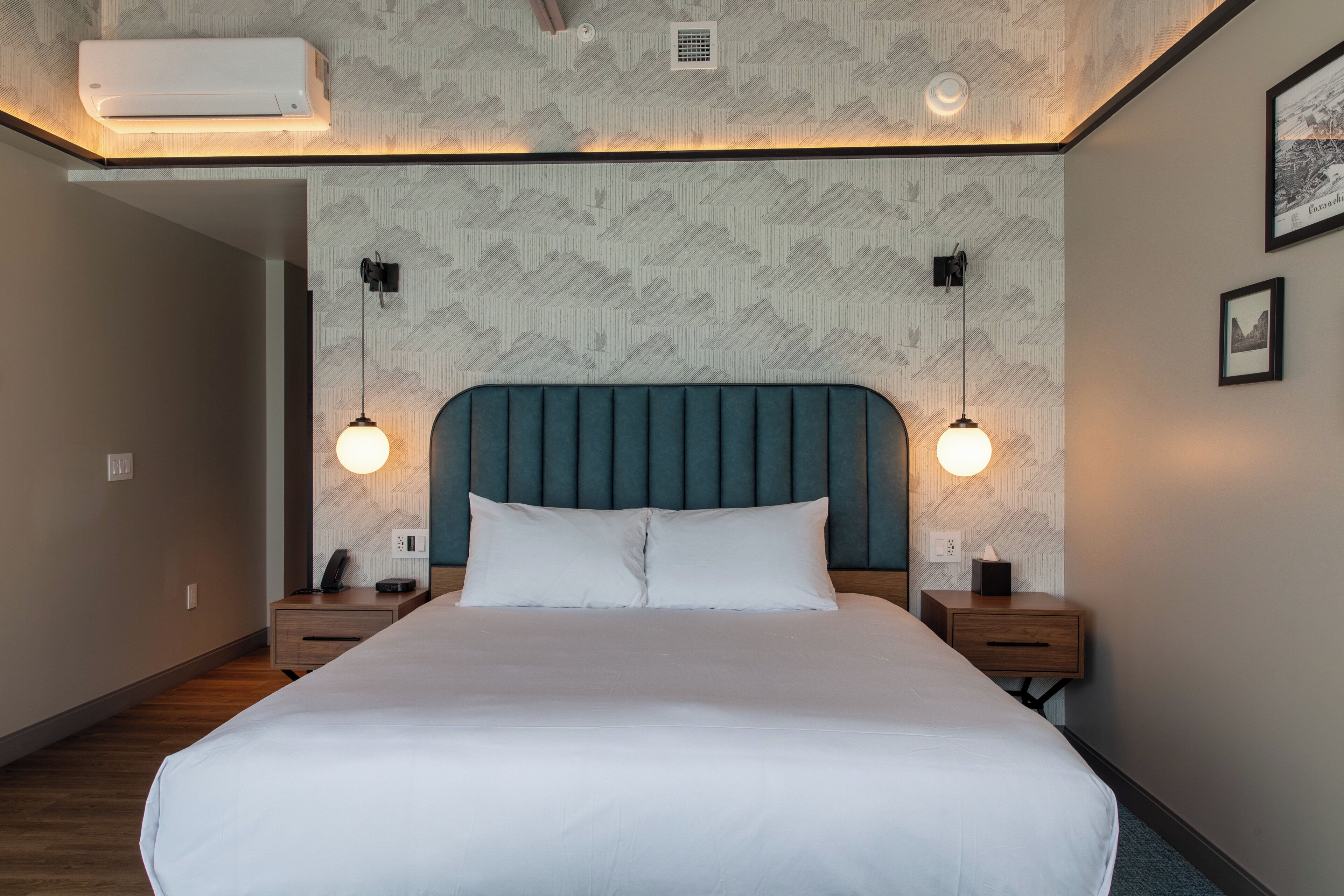 Quarto de hotel com uma cama grande, duas mesas de cabeceira, um painel de cabeceira e uma parede com padrão.
