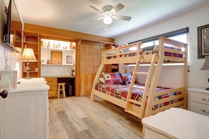 Quarto com beliche, ventoinha no teto, móveis de madeira e escrivaninha com abajur.
