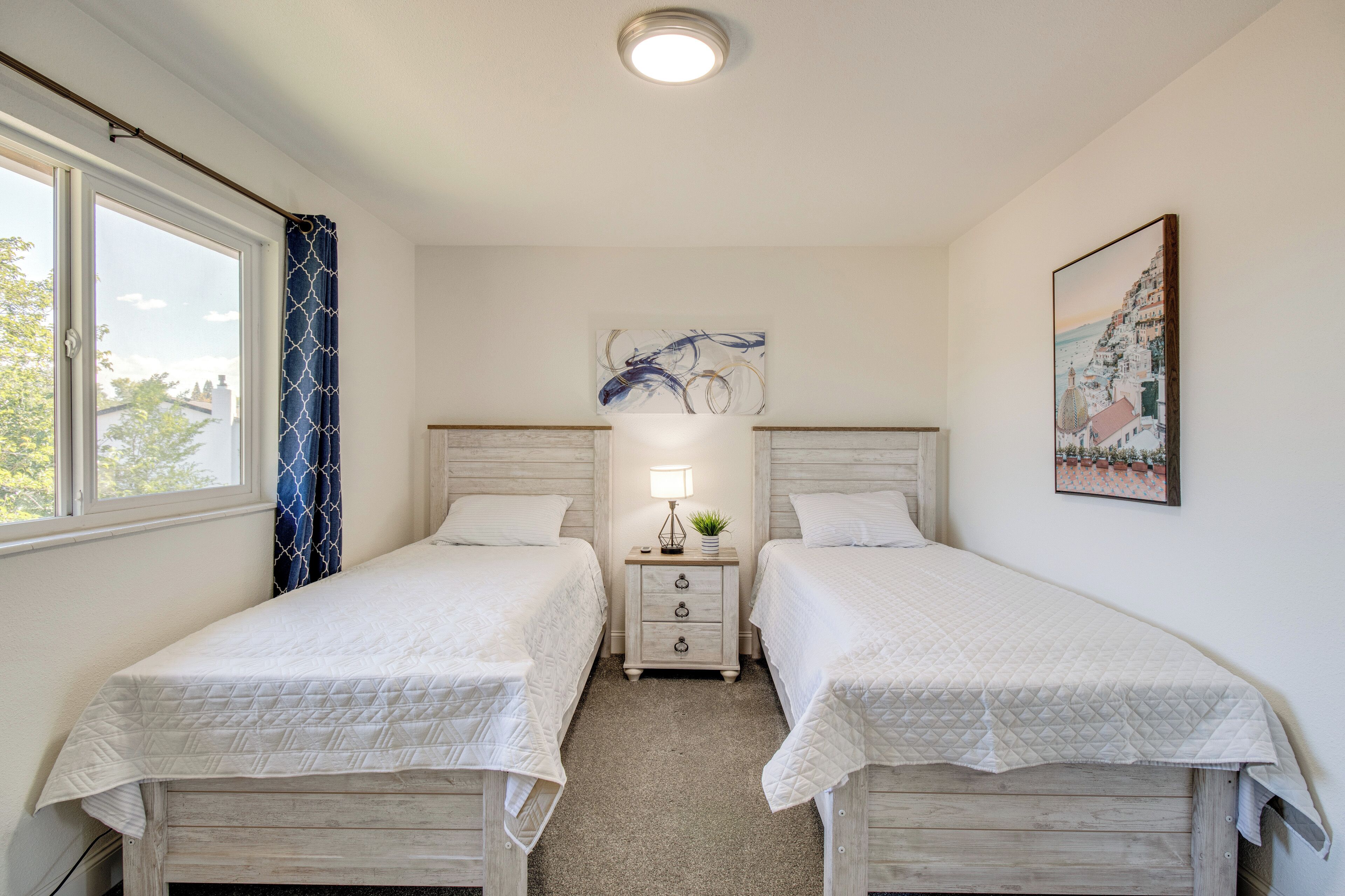 Quarto com duas camas, mesa de cabeceira com abajur e um quadro na parede.