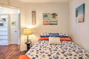 Quarto com cama, mesa de cabeceira, abajur e quadros na parede.