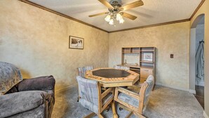 Um quarto com uma mesa hexagonal, seis cadeiras estofadas, um ventilador de teto e piso coberto de carpete.