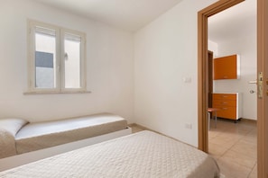 Quarto com duas camas, uma janela e porta que dá para um banheiro.