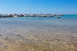 Um cais com barcos atracados, água rasa e cristalina, e um mar calmo.