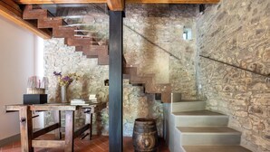 Um interior rústico com parede de pedra, escada de madeira e uma mesa com livros e um vaso.