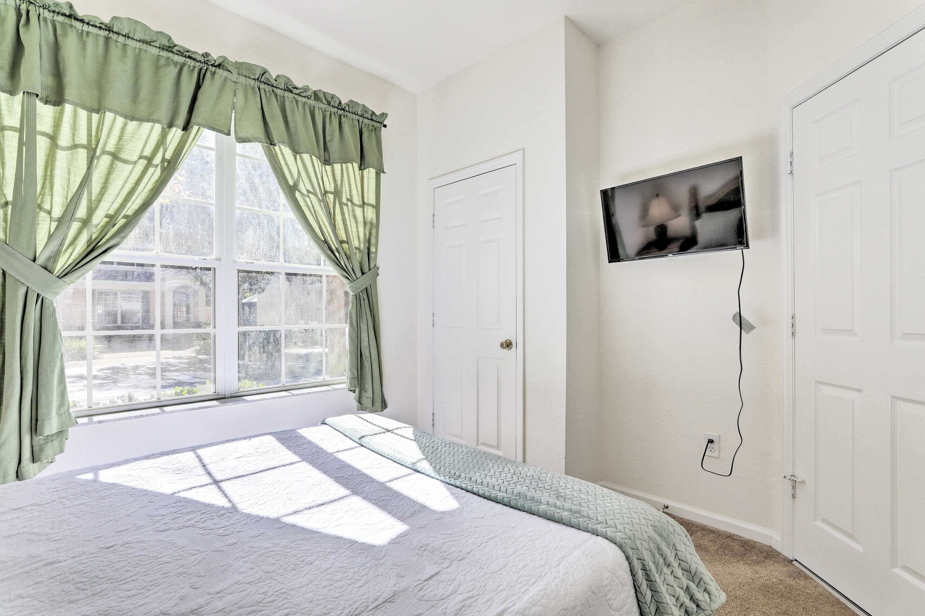 Quarto com cama, janela com cortinas, televisão na parede e uma porta.