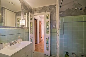 Casa de banho com lavatório branco, espelho e área de chuveiro com azulejos verdes.
