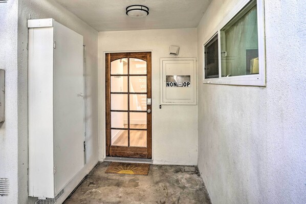 Um corredor estreito com uma porta de madeira, uma porta branca com uma placa 'NÃO OPERACIONAL' e uma janela com vista para a rua.