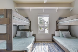 Quarto com beliches, janela com persianas e tapete listrado.