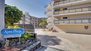 Um edifício de vários andares com varandas, uma placa com a inscrição "Kona Plaza" e um calçadão.