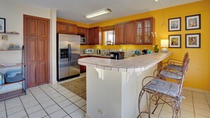 Cozinha com armários de madeira, geladeira de aço inoxidável, micro-ondas e ilha com banquetas.