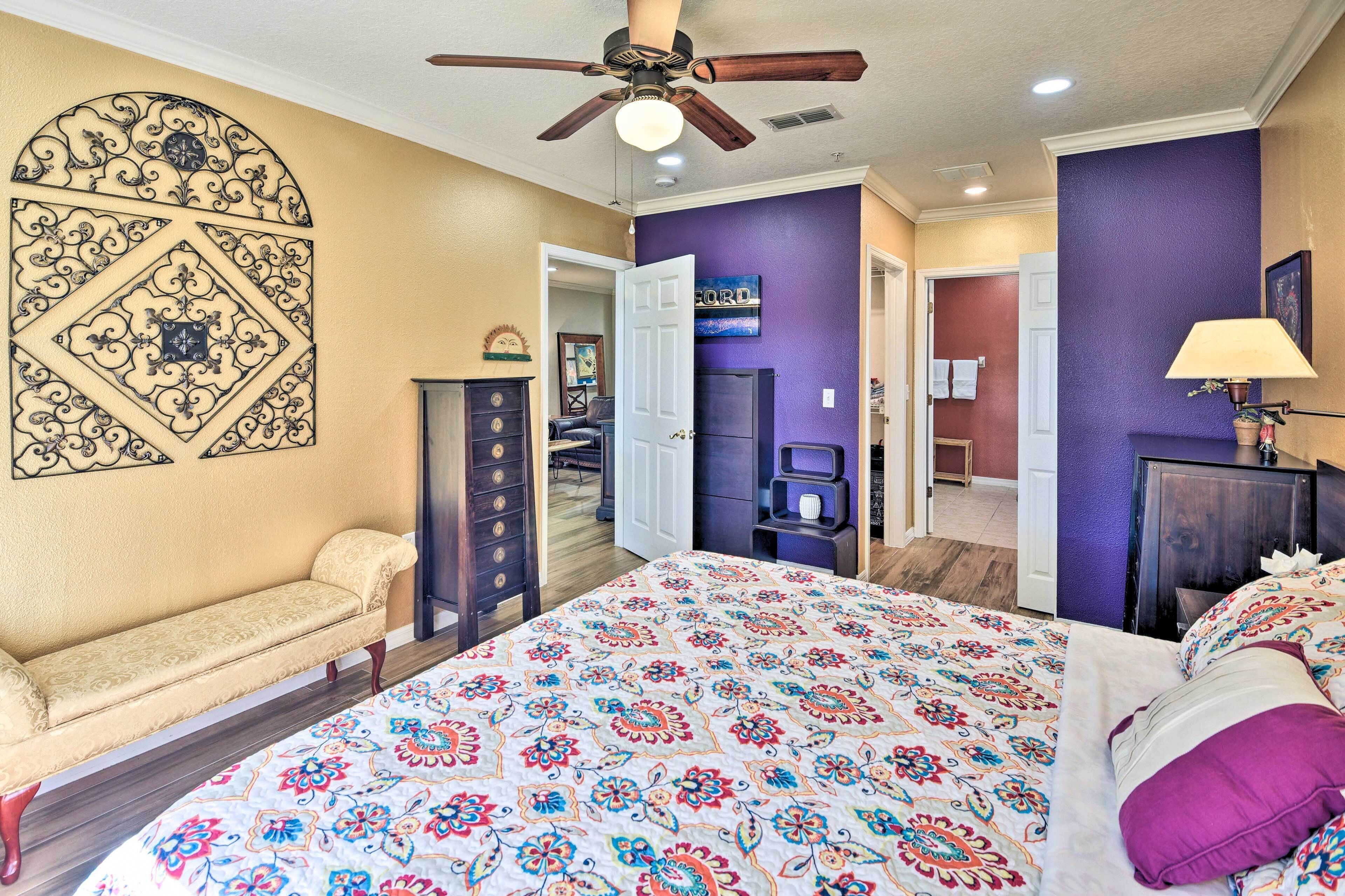 Quarto com uma cama grande, um ventilador de teto, um sofá e um objeto decorativo na parede.