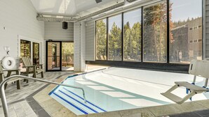 Uma área interna de piscina moderna com janelas de vidro transparente, piscina com azulejos azuis e uma cadeira à beira da piscina.