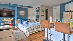 Quarto com cama, escrivaninha, cadeira, televisão, estante de livros e banheiro com espelho e pia.
